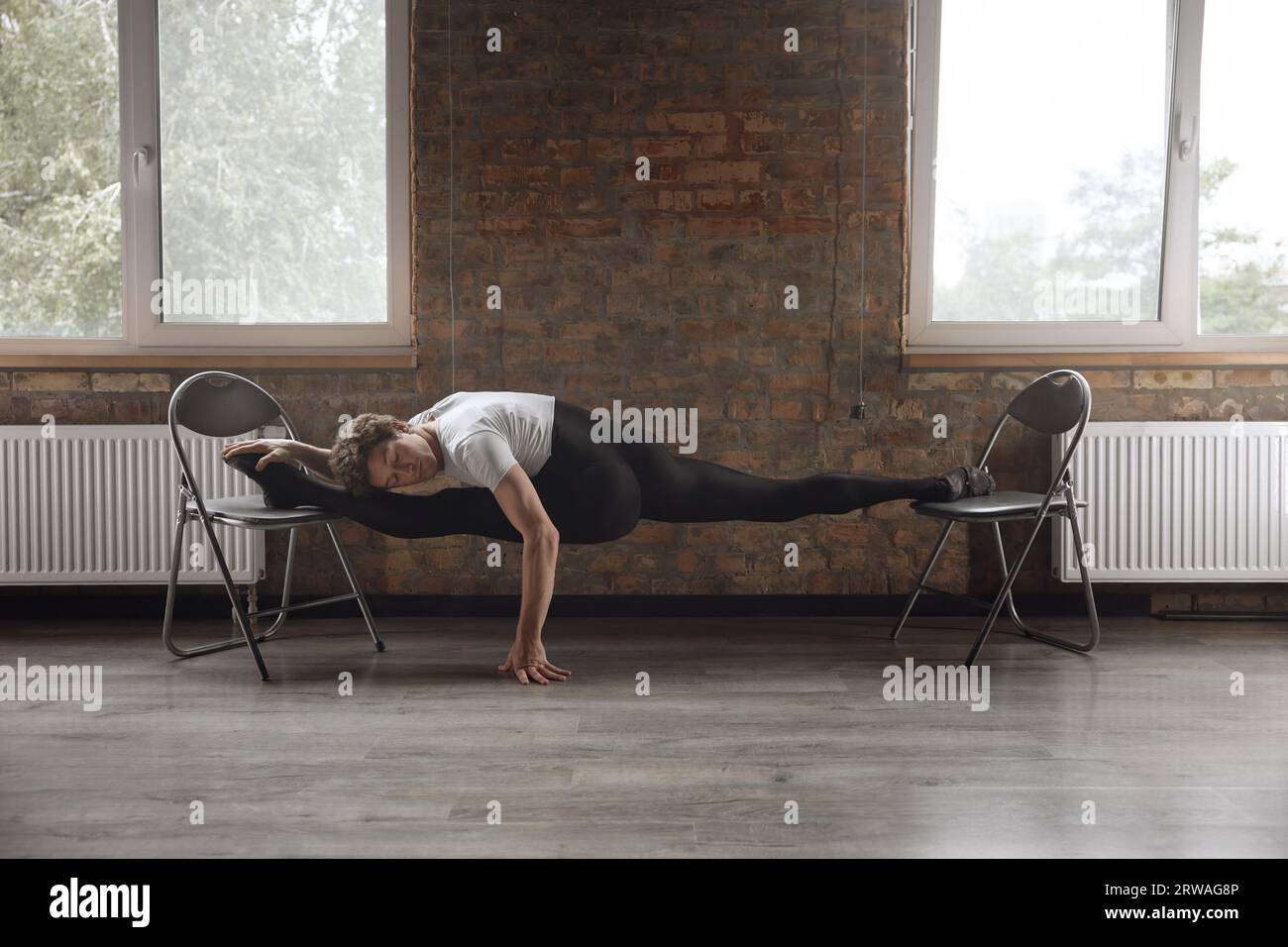 Man ballet dancer doing stretching performing split with two chairs ...