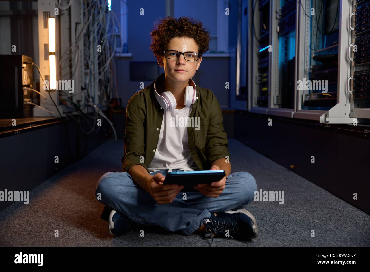 Teenager IT worker sitting on floor of modern server room working on ...