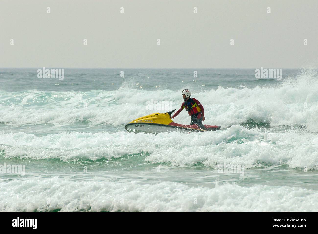 RNLI lifeguard member on rough seas off Perranporth Beach, Cornwall, UK ...