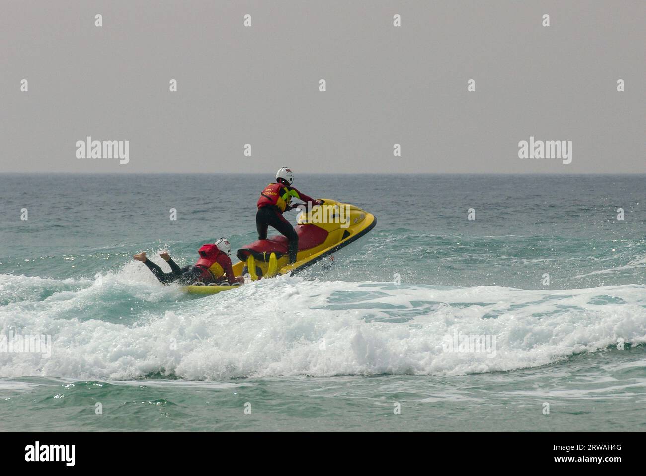 RNLI lifeguard member on Jet ski with another on a rescue sled heading ...