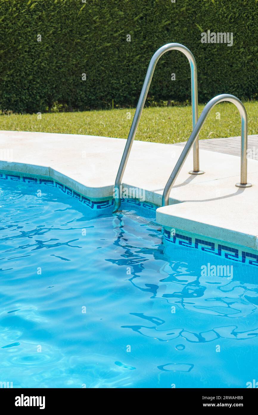 Swimming pool curb with ladder, with cool blue looking water and a bush ...