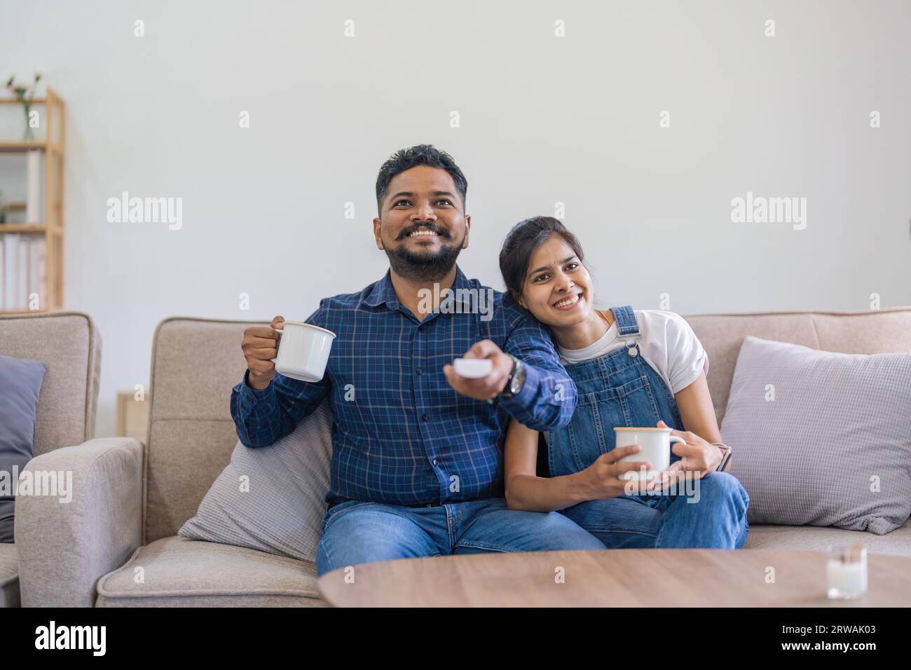 Indian couple watch tv on the couch at their living room, husband and ...