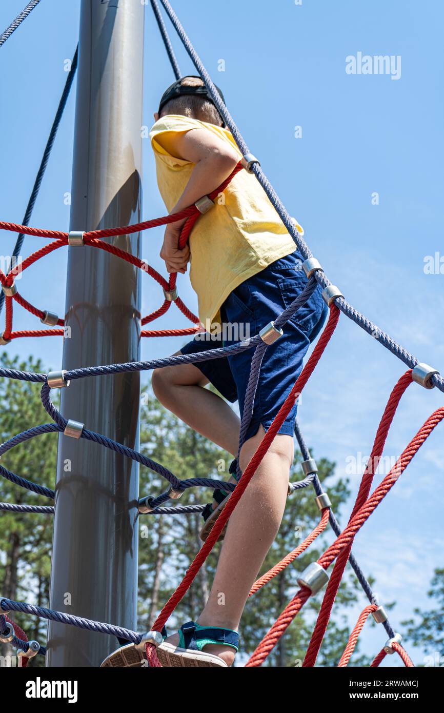 Boy climbing on a rope climbing frame in a playground in summer ...