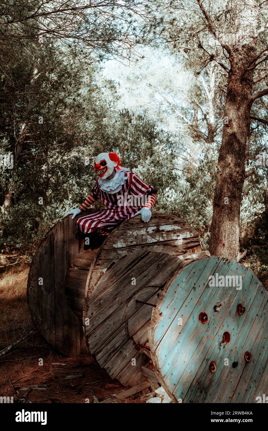a mad evil redhead clown in the woods, wearing a white and red striped ...