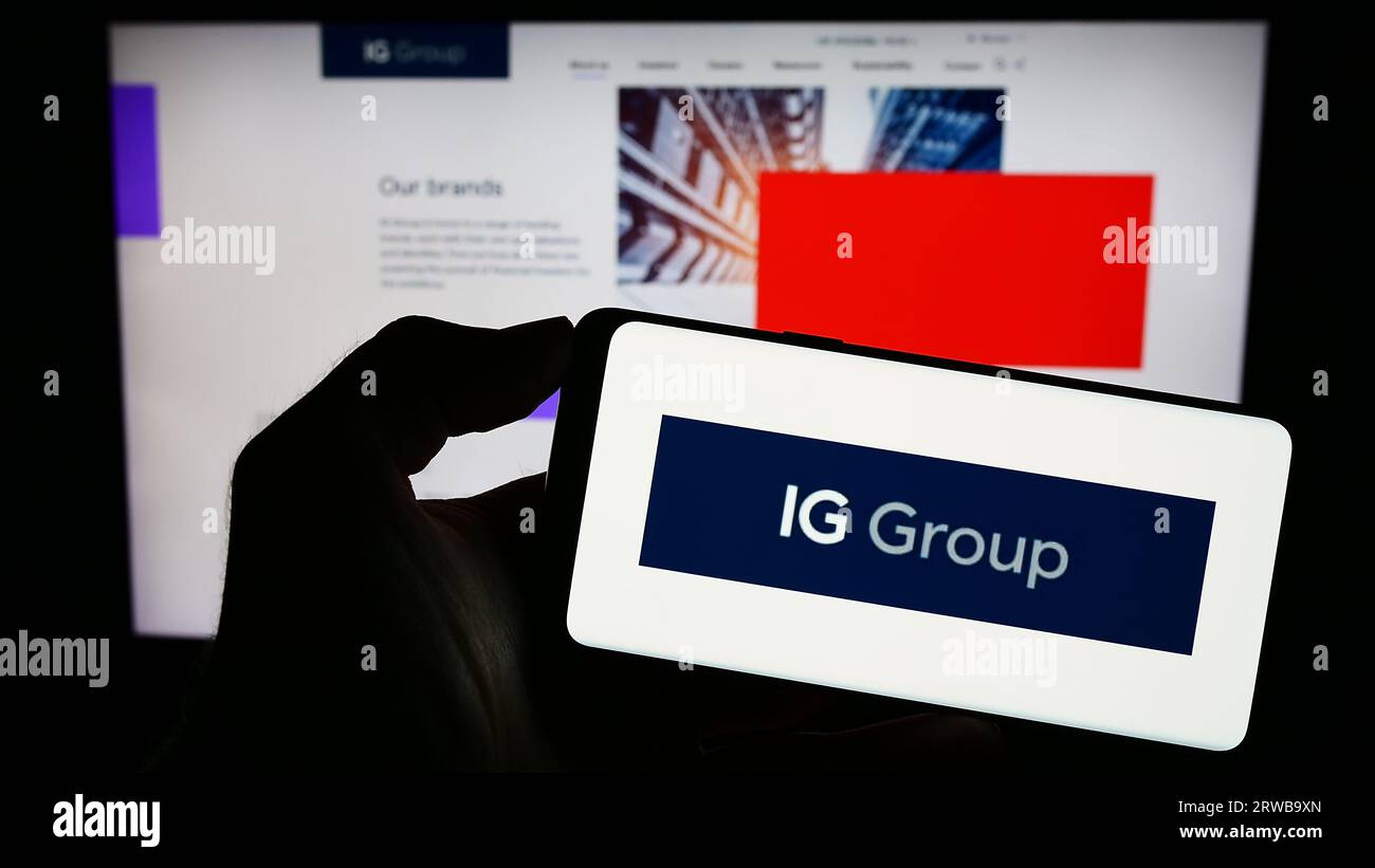 Person holding smartphone with logo of British trading company IG Group Holdings plc on screen ...