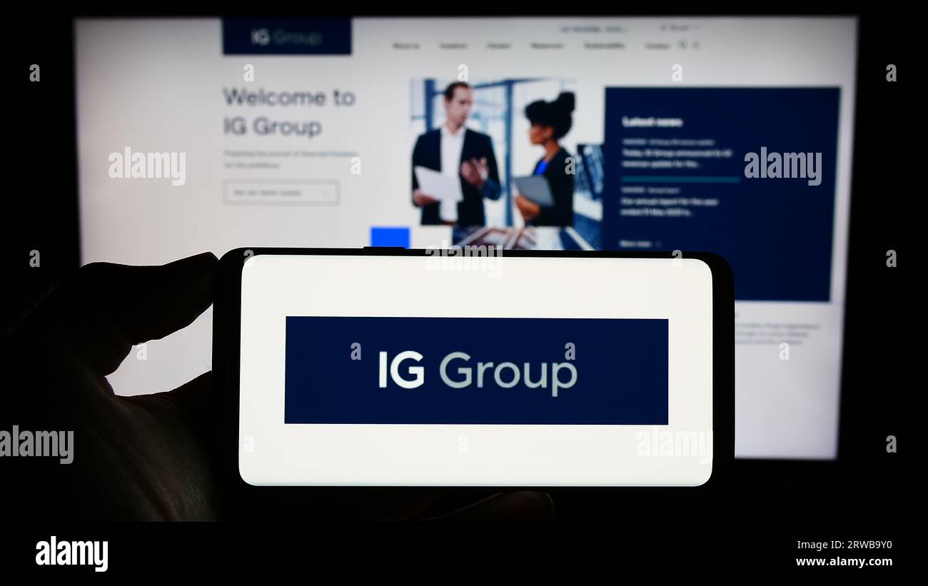 Person holding cellphone with logo of British trading company IG Group Holdings plc on screen in ...