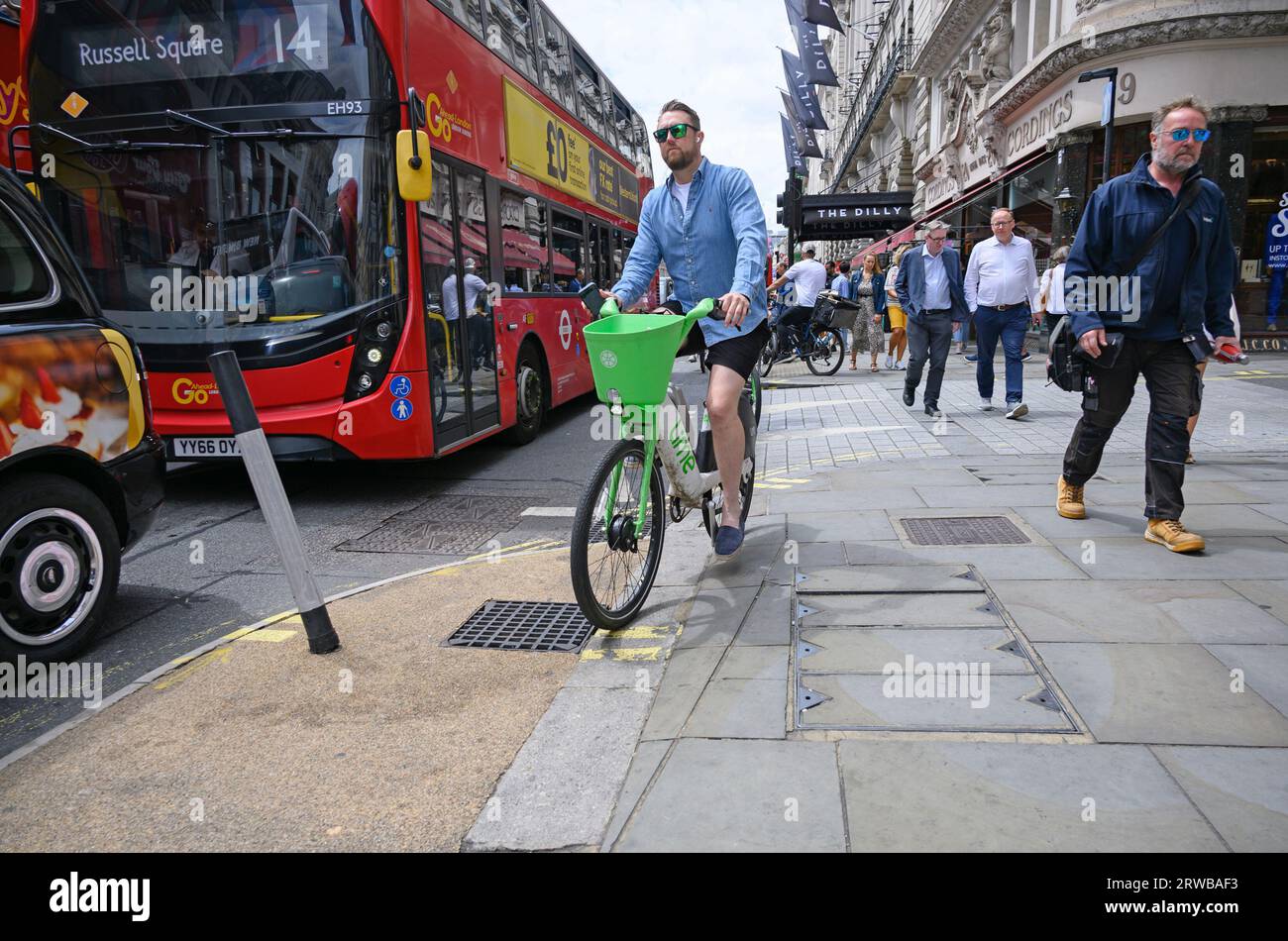 London, UK. Man cycling on the pavement in Piccadilly on a Lime rental ...
