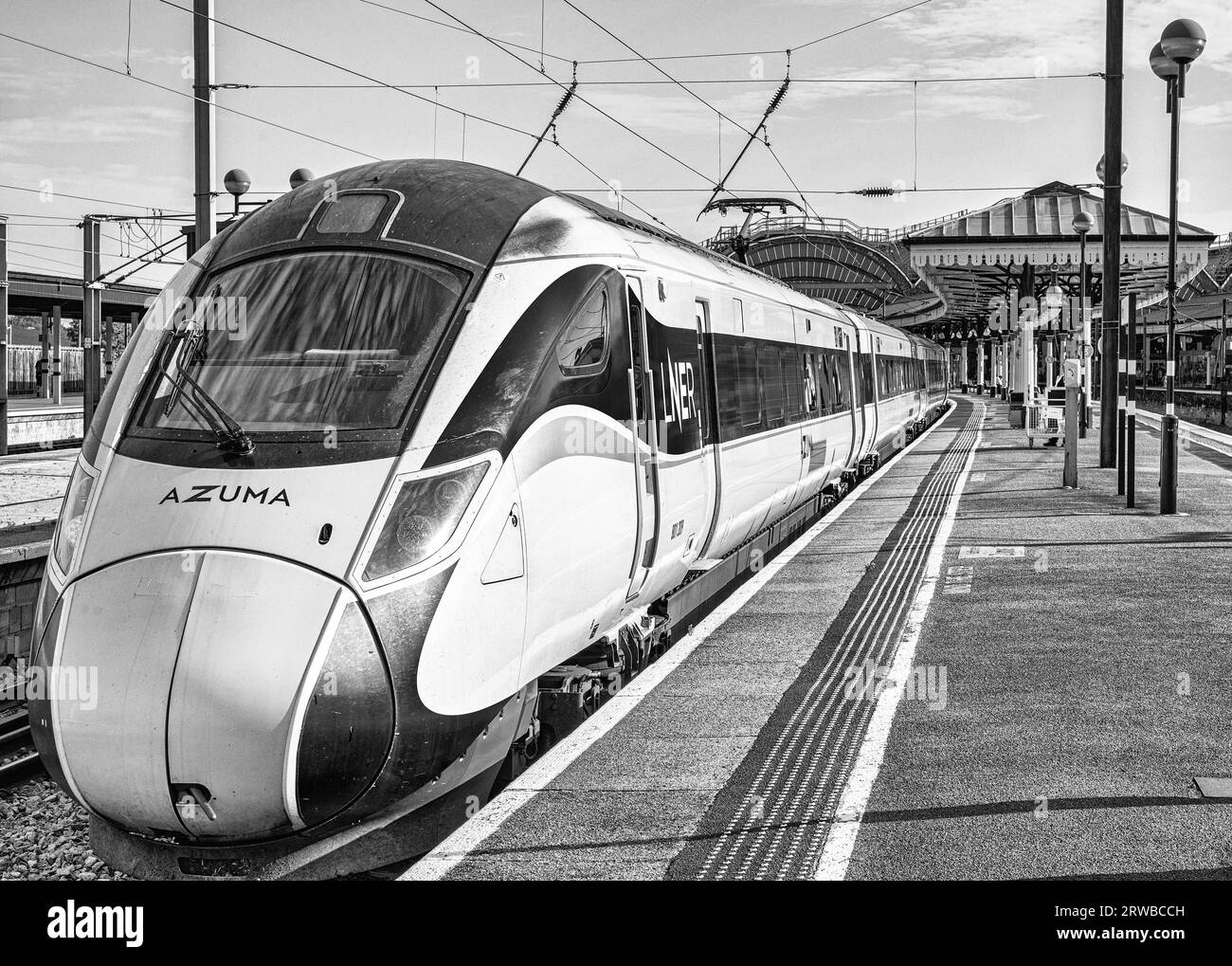 A train stands at a railway station platform with a historic 19th ...