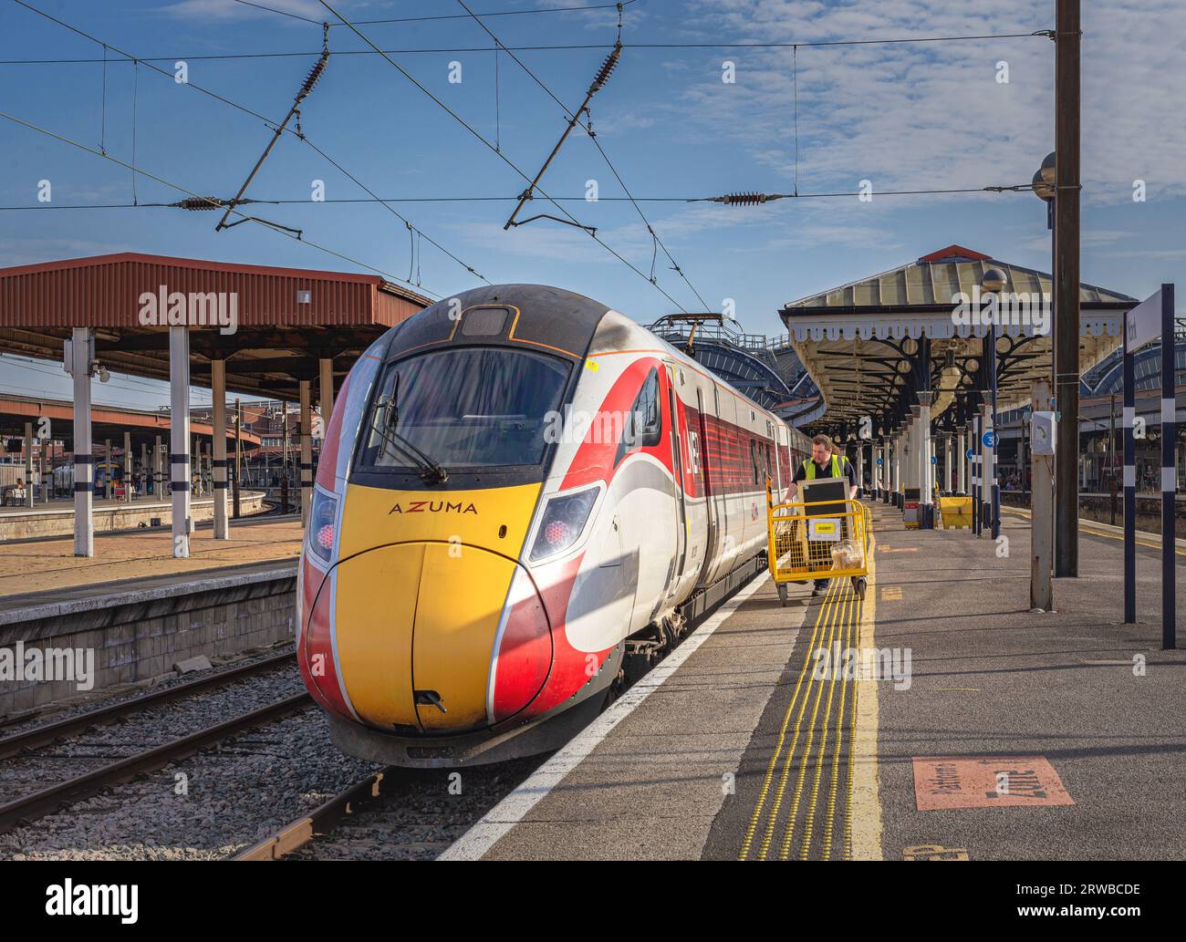 A train stands at a railway station platform with a historic 19th ...