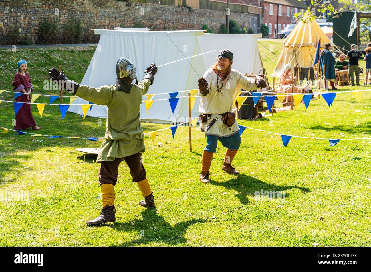 Two men in period costume, jousting with swords in the sunshine during ...