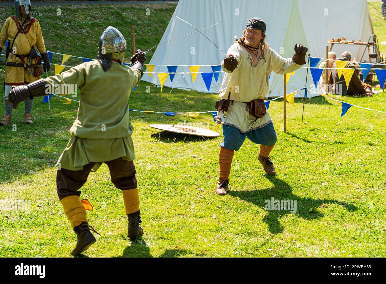 Two men in period costume, jousting with swords in the sunshine during ...