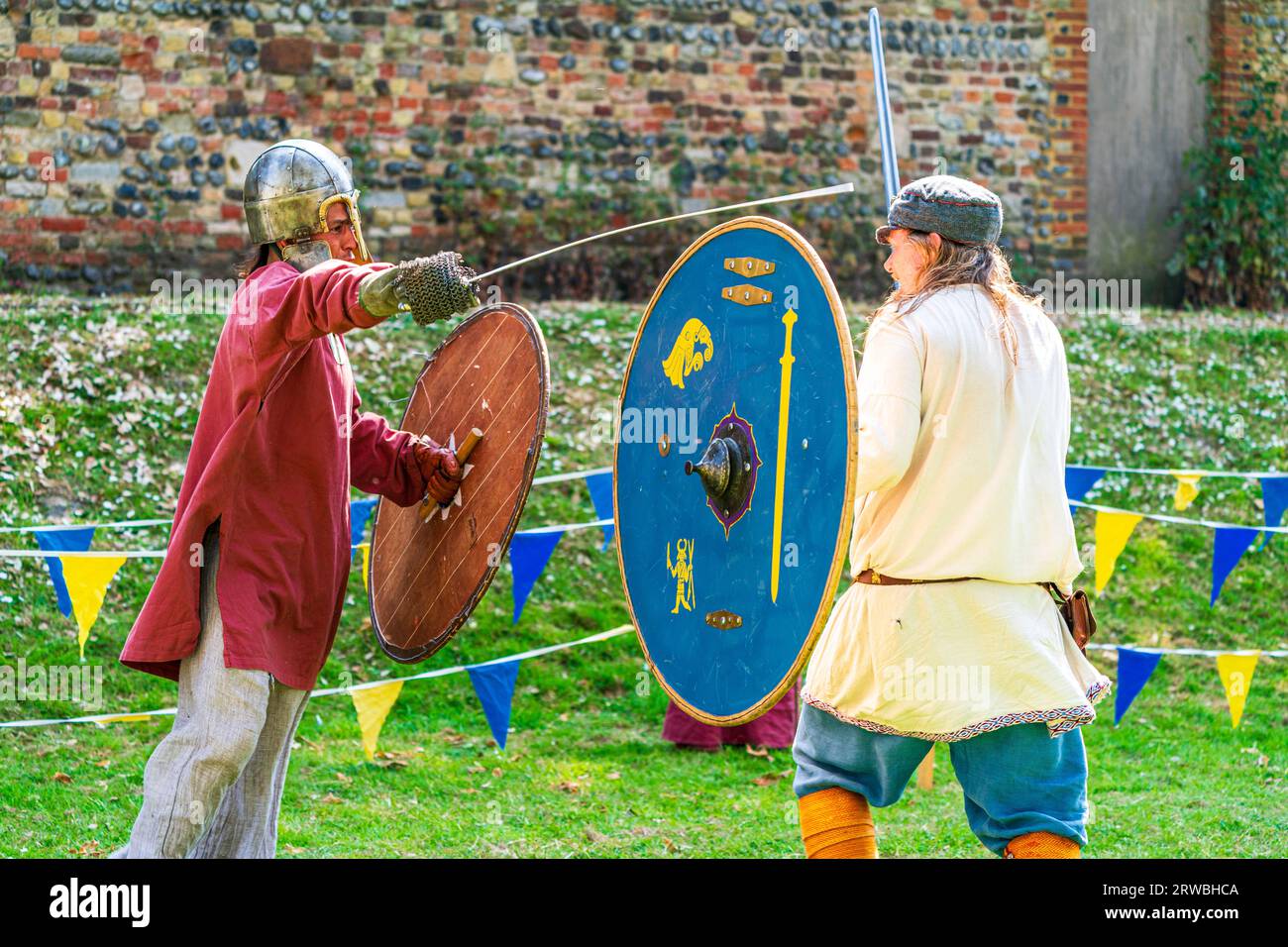 Two men in period costume, jousting with swords in the sunshine during ...