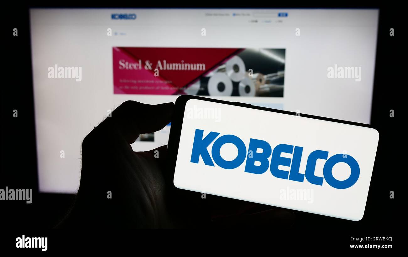 Person holding mobile phone with logo of Japanes company Kobe Steel Ltd. (Kobelco) on screen in ...