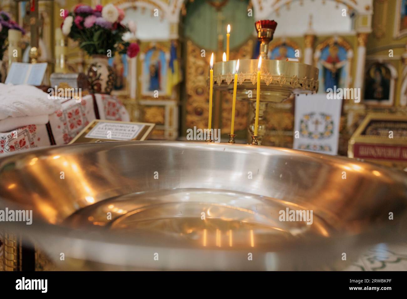 Baptismal font with blessing water and wax candles are against background of Orthodox church ...