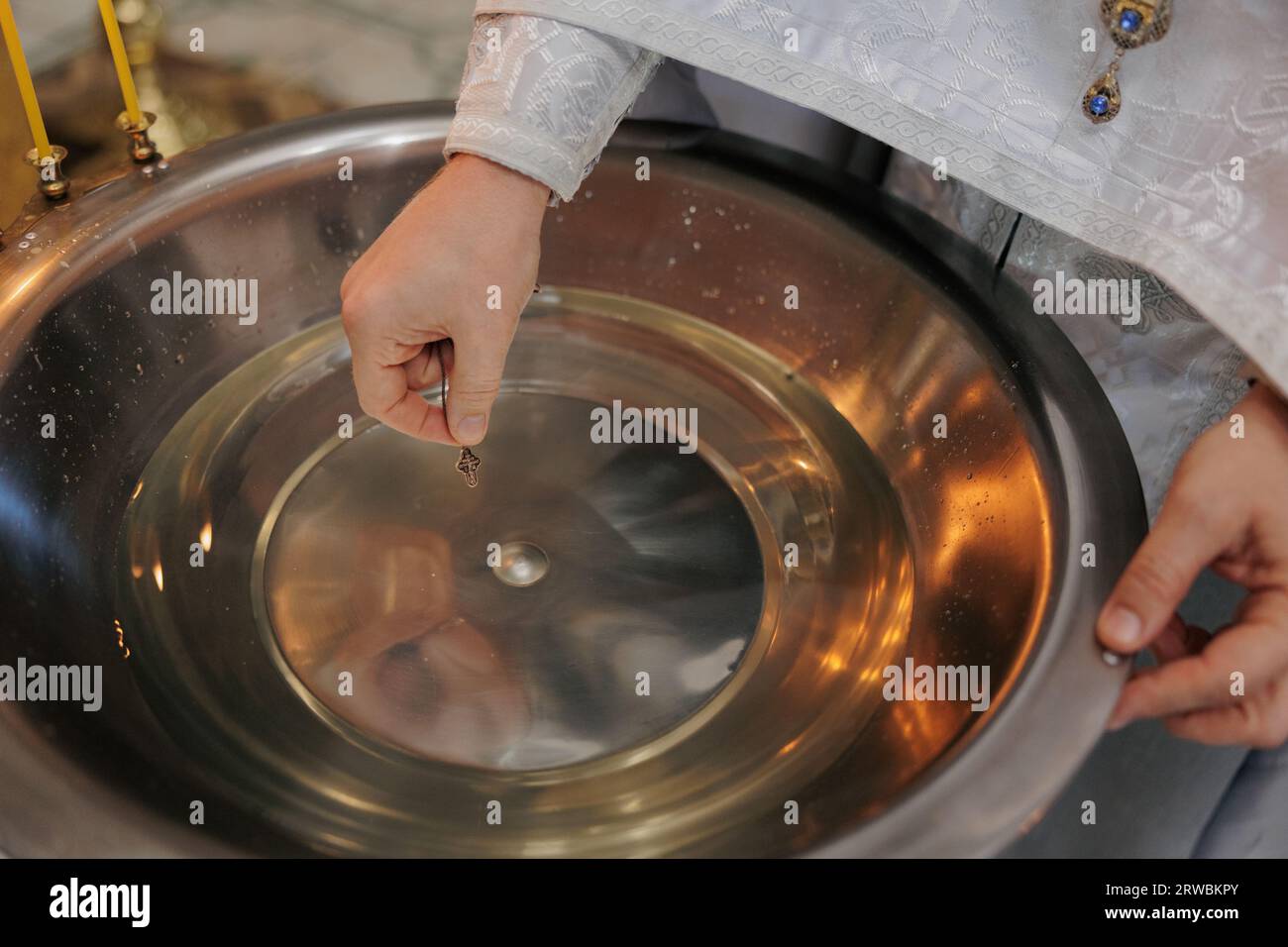 Closeup view to the priest hand holding cross and baptismal font with water. Ceremony of the ...