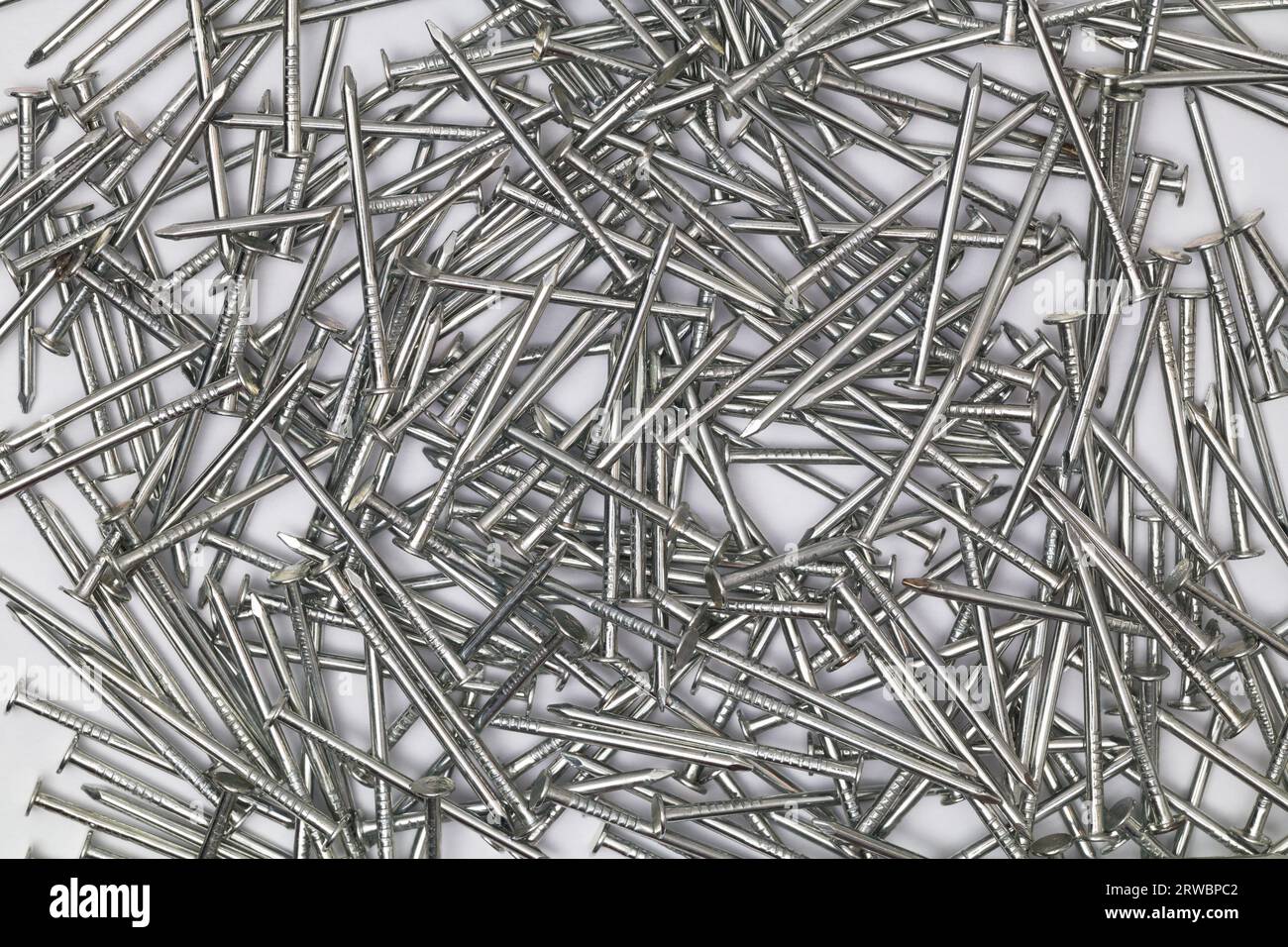 The photo displays a collection of nails scattered on a clean white ...