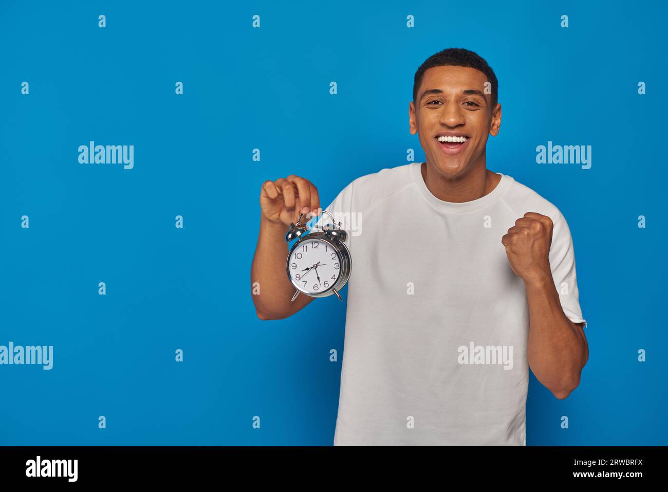 excited african american man with open mouth holding alarm clock on ...