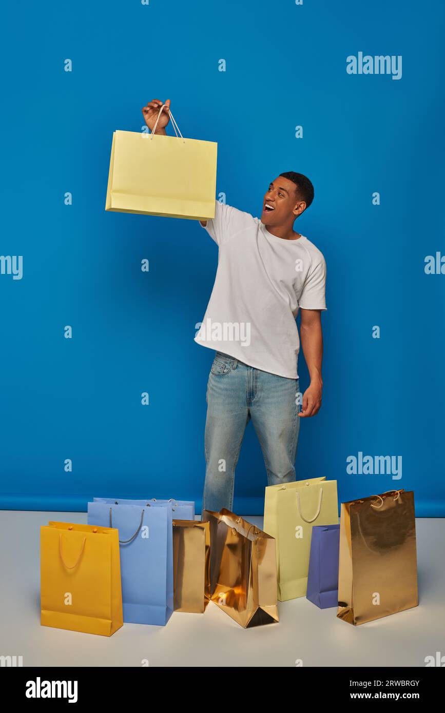excited african american man in casual attire holding shopping bags on ...