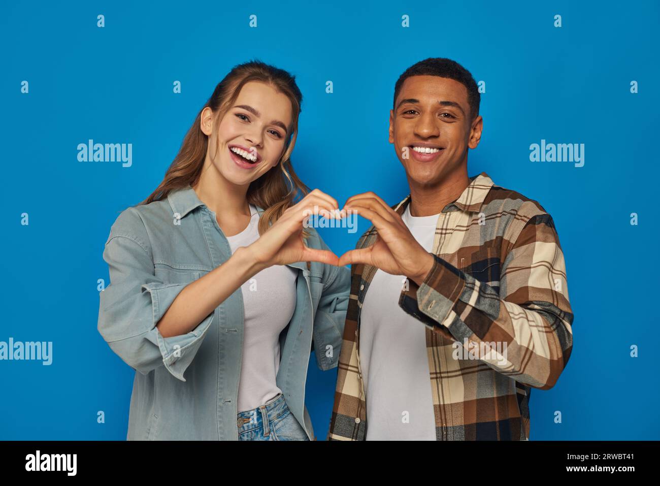 cheerful interracial couple showing heart sign with hands and looking ...