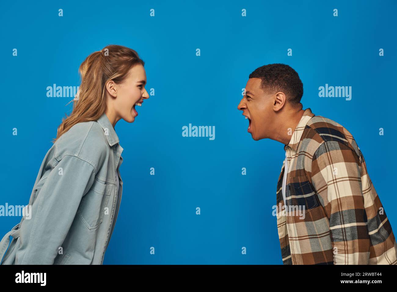 multicultural couple screaming at each other on blue backdrop, arguing ...