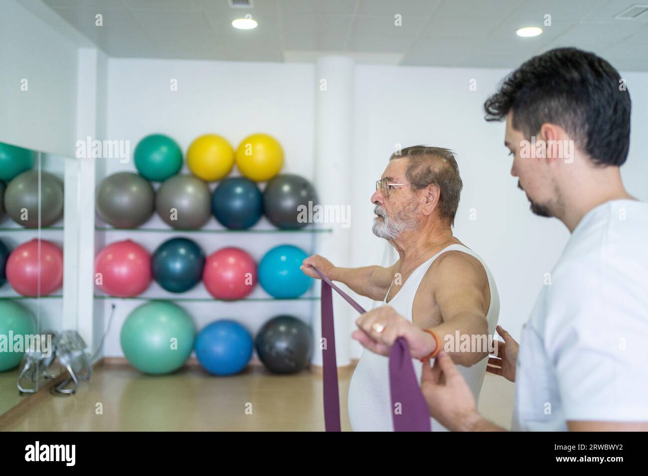 Serious male therapist in uniform helping senior patient to do exercise ...