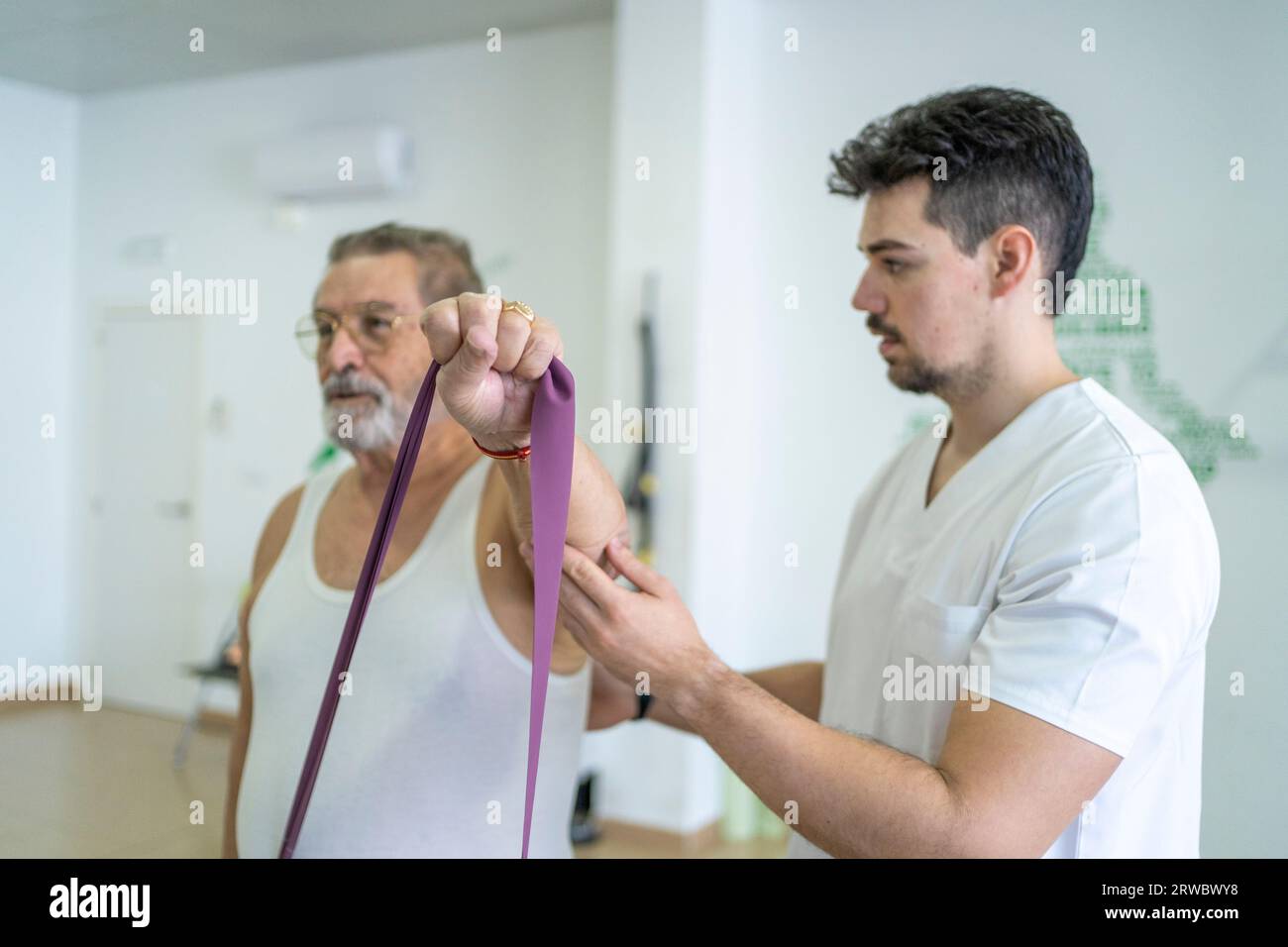 Serious male therapist in uniform helping senior patient to do exercise ...
