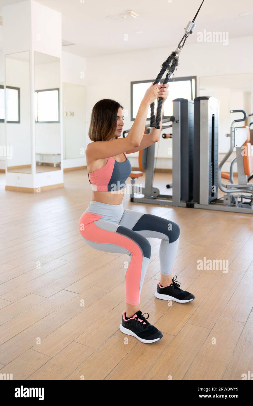 Full body of young athletic woman performing lateral pulldowns in squat ...