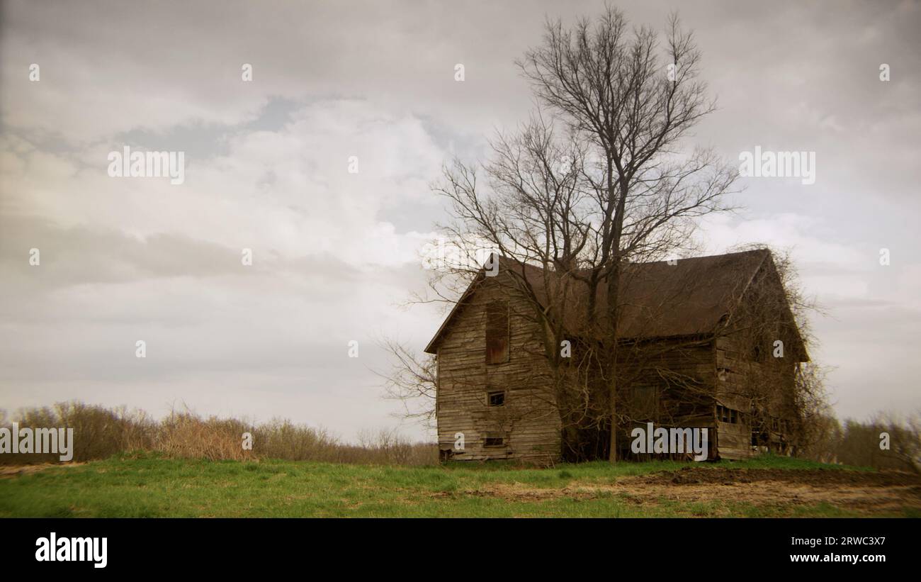Spooky and long abandoned farm house shares a field with a dead tree as ...