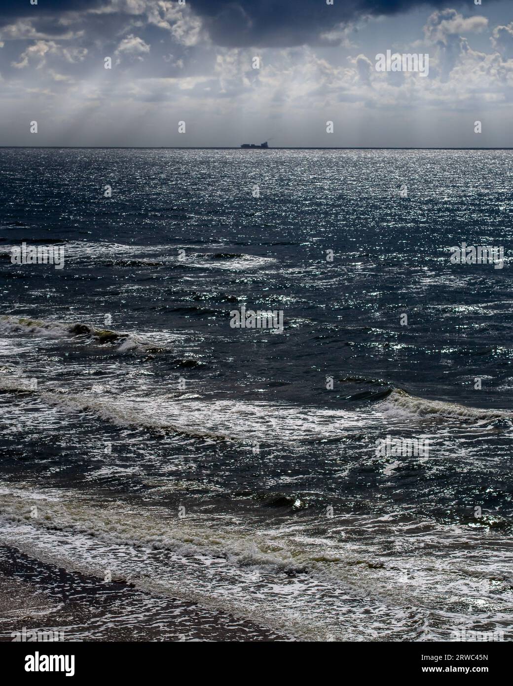 Baltic Sea, midday, the sun's rays break through the clouds and a ship ...