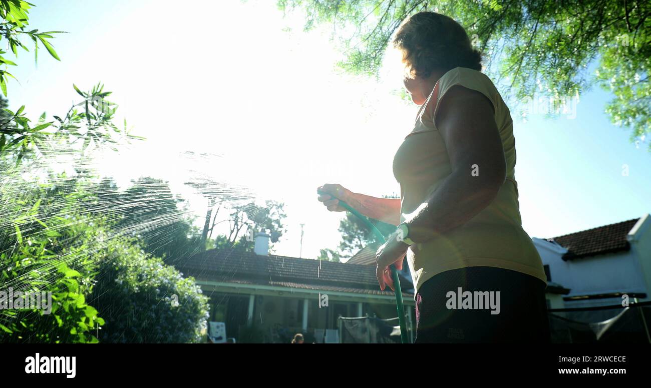 Relaxed senior lady watering plants outside in sunlight Stock Photo - Alamy