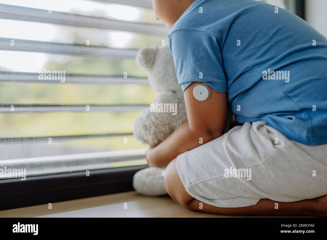 Diabetic boy with a continuous glucose monitor sitting by the window ...