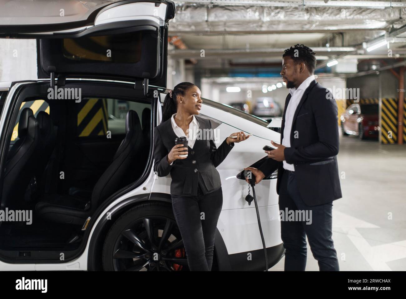 Business people with phones preparing EV for drive in garage Stock ...