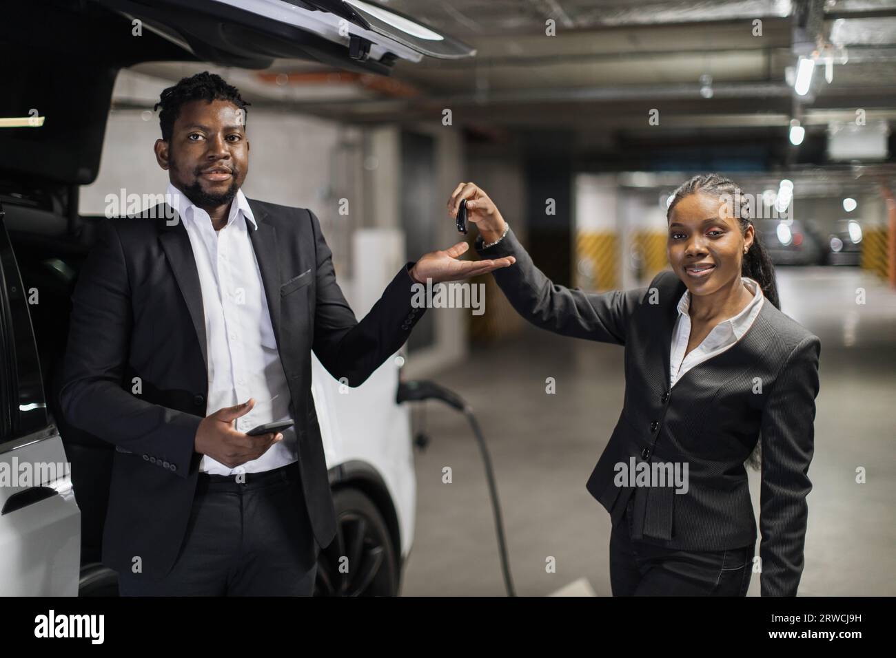 Female handing EV keys to male buyer in below-ground parking Stock ...