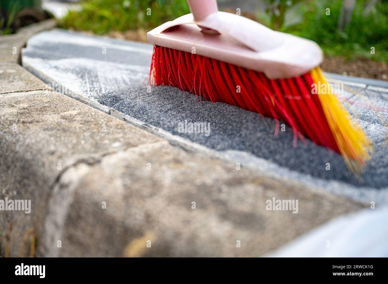 Low angle closeup view of bright red broom pushing a tile gap sand into ...