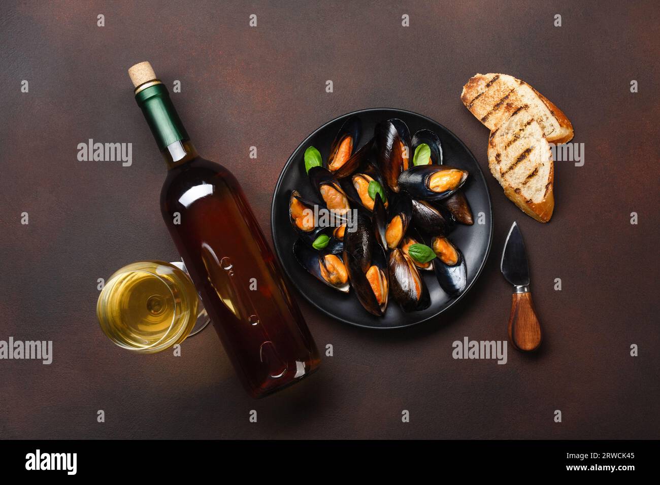 Seafood mussels and basil leaves in a black plate with wine bottle ...