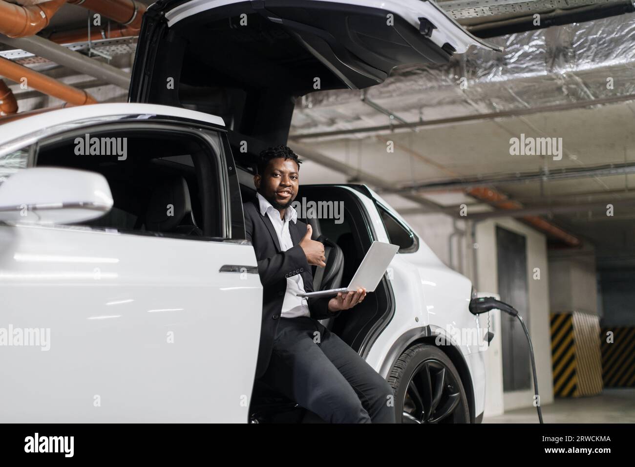Adult typing on computer inside EV during fill-up in garage Stock Photo ...