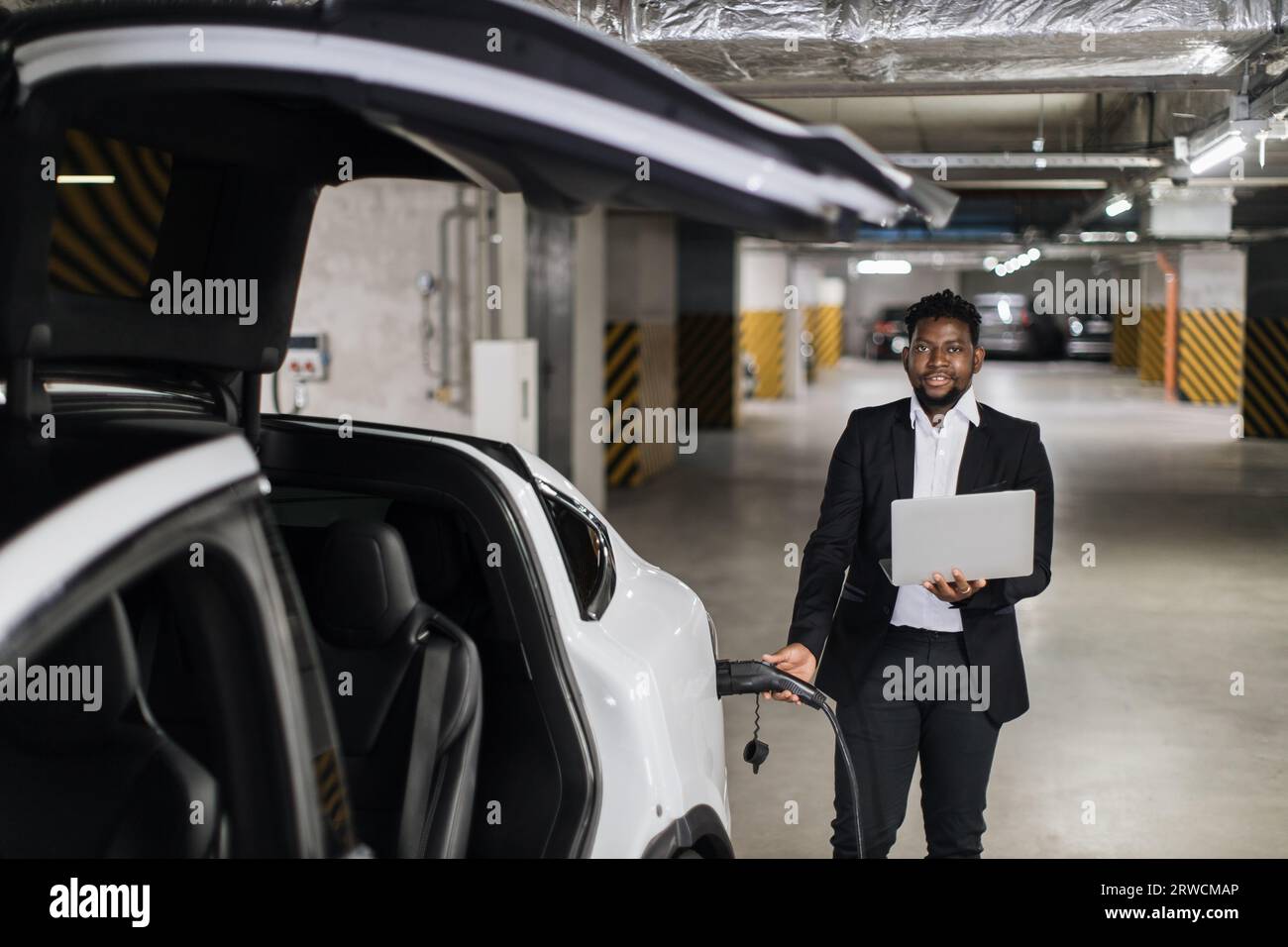 Man with computer plugging in EV charging cord in parking Stock Photo ...