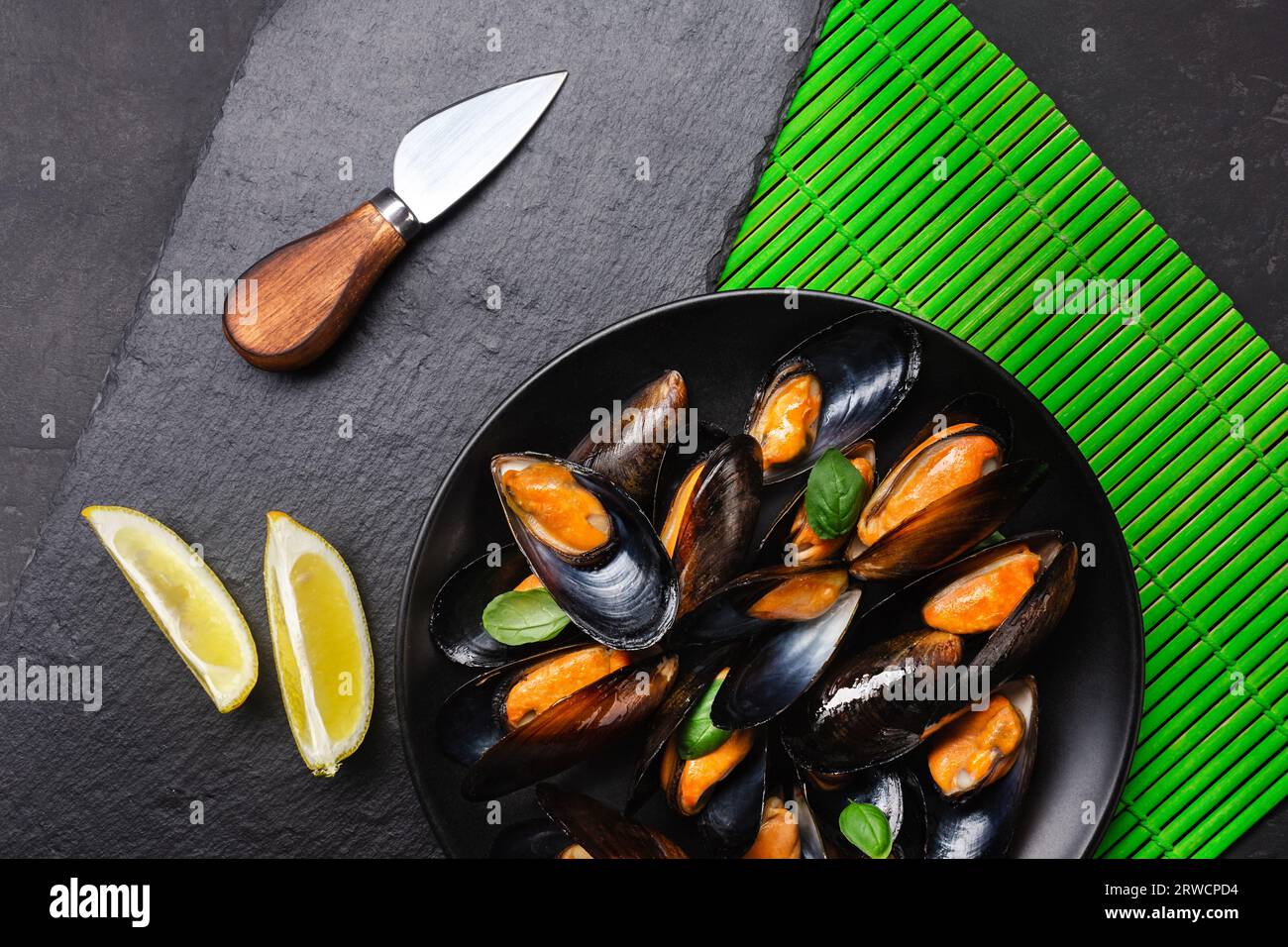 Seafood mussels, basil leaves in a black plate with lemon and knife on ...