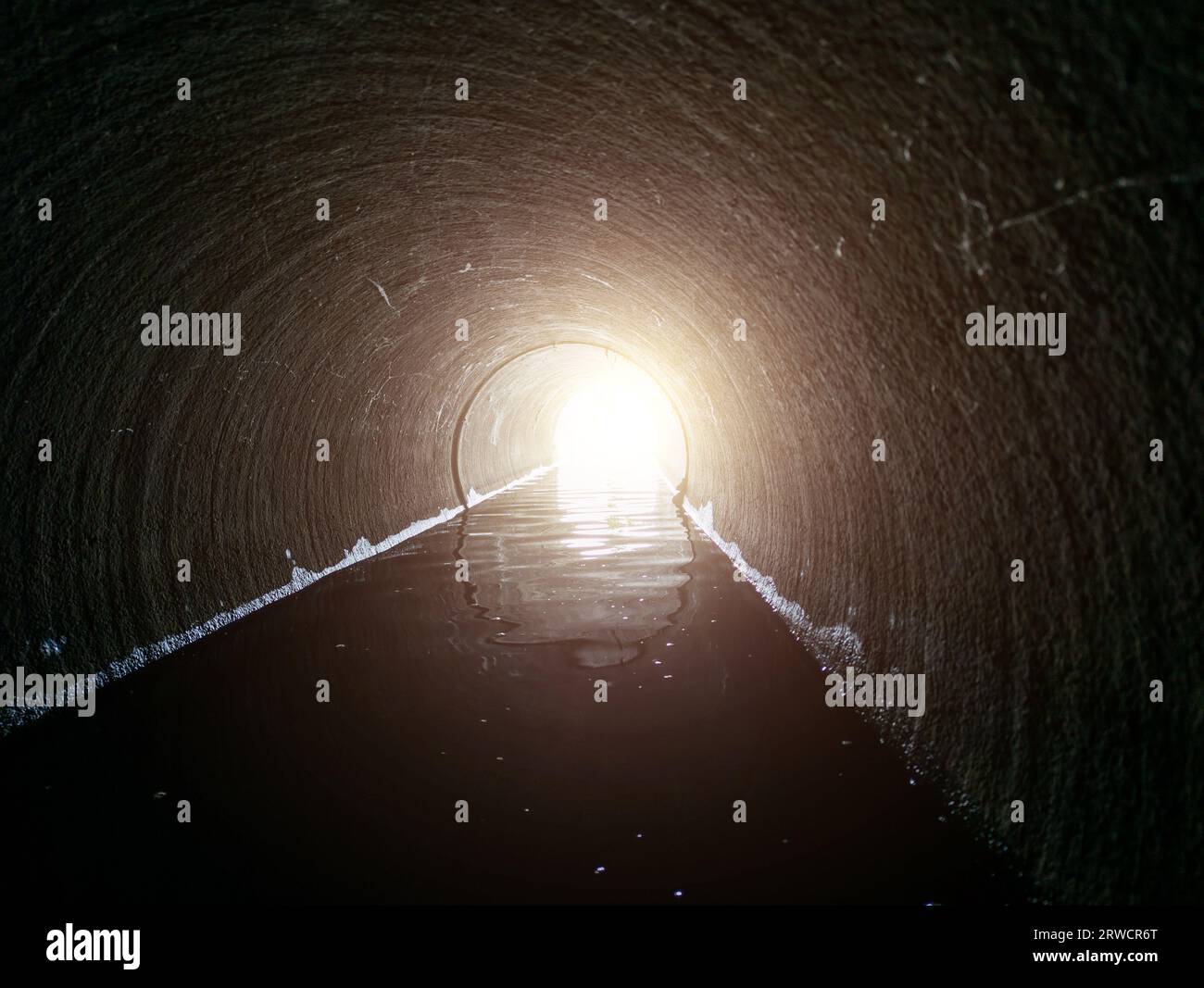 Light at end of round flooded sewer tunnel. Exit from sewer system ...