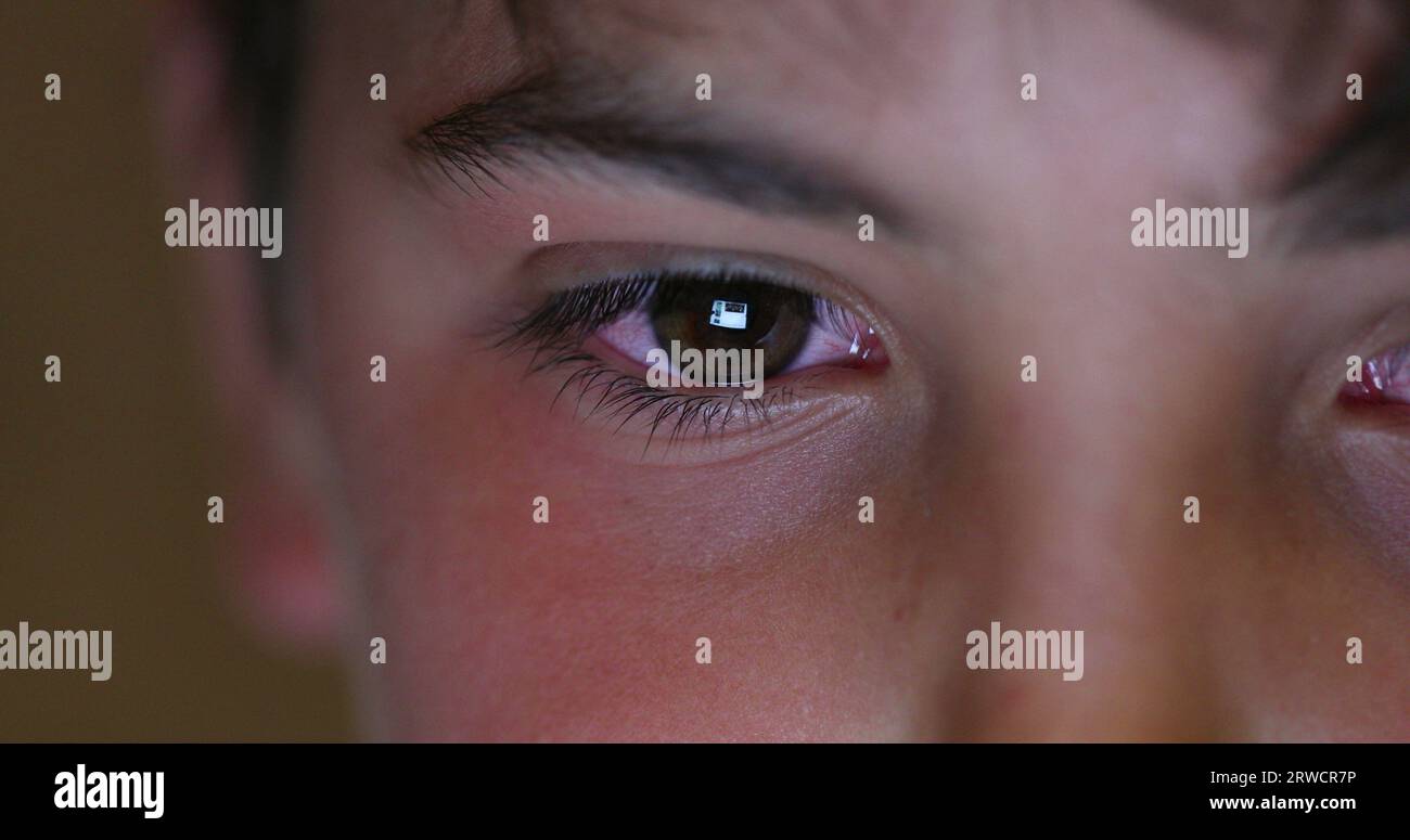 Young boy eyes staring at screen at night. Close-up of child face ...