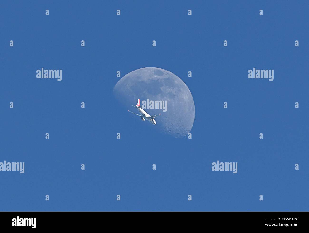 A passenger jet flies across the moon, set against a blue sky Stock ...