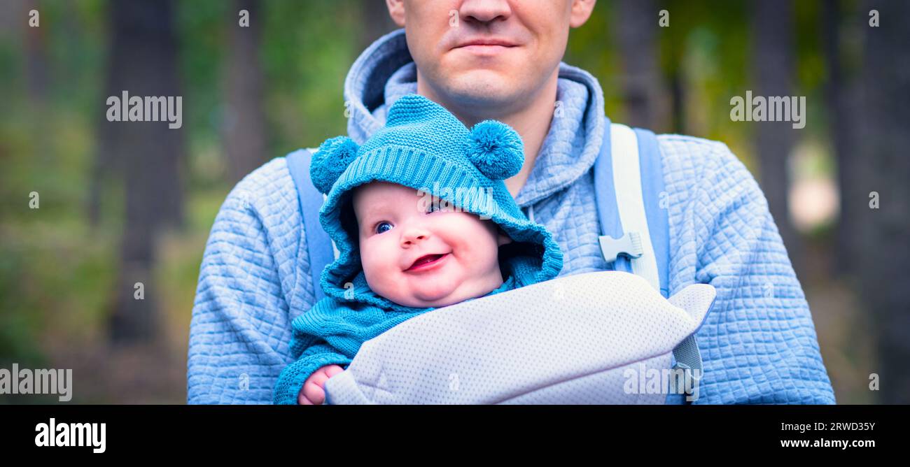 Young father with his newborn baby in a sling walking in the autumn ...