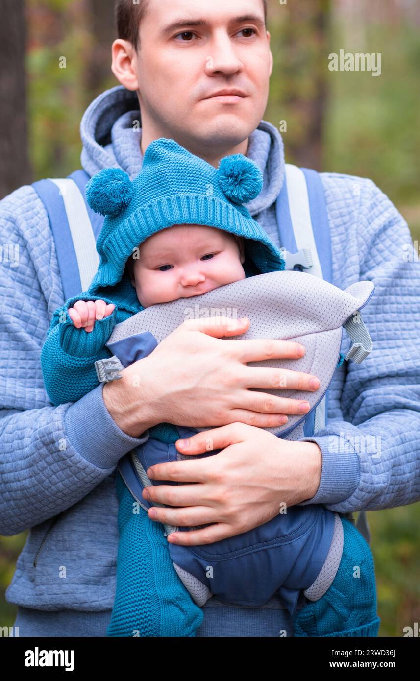 Young father with his newborn baby in a sling walking in the autumn ...