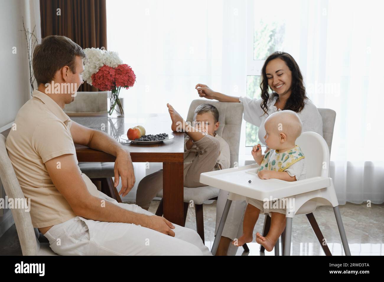 Family with children eating by the table at home. Mother feeding ...
