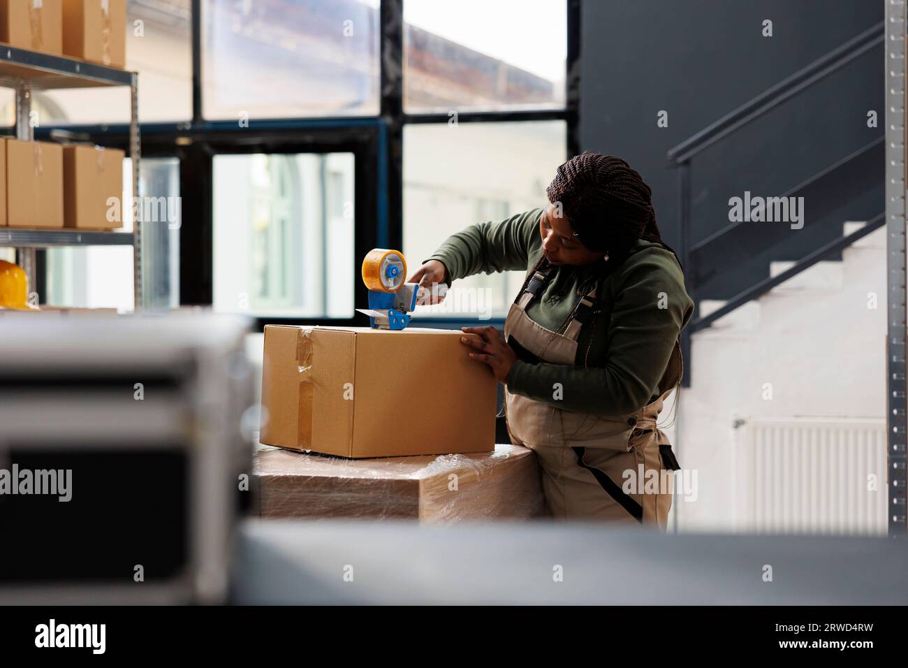 African american supervisor using adhesive tape in warehouse, working ...