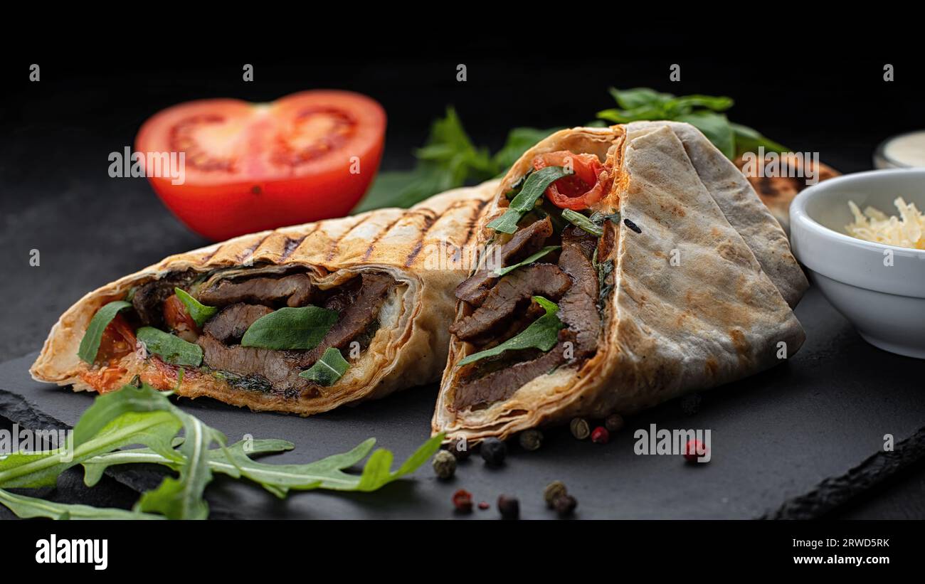 Shawarma with meat, cheese, tomatoes and sauce, on a black background ...