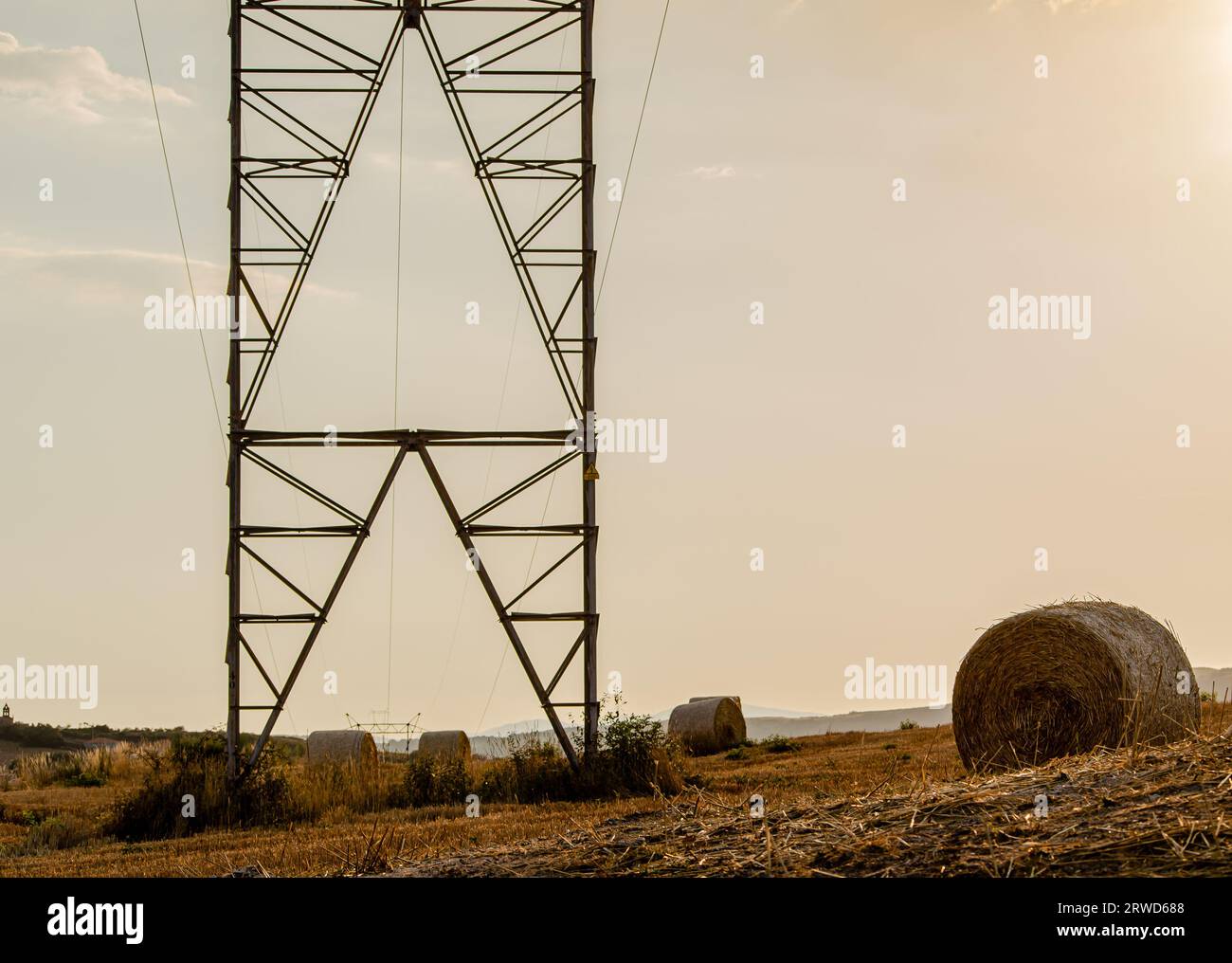 high voltage pylon in a mowed field with straw rollers at sunset Stock ...