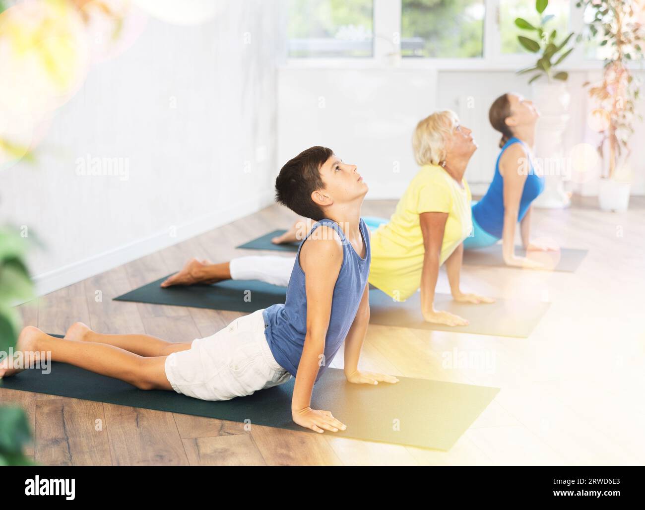 Mother, grandmother and teen son do exercise upward facing dog pose ...