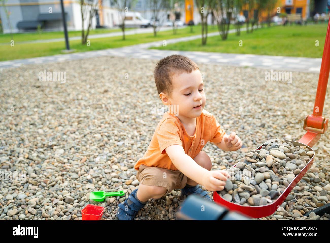 Little toddler boy playing with toys on pebbles on the playground. Boy ...