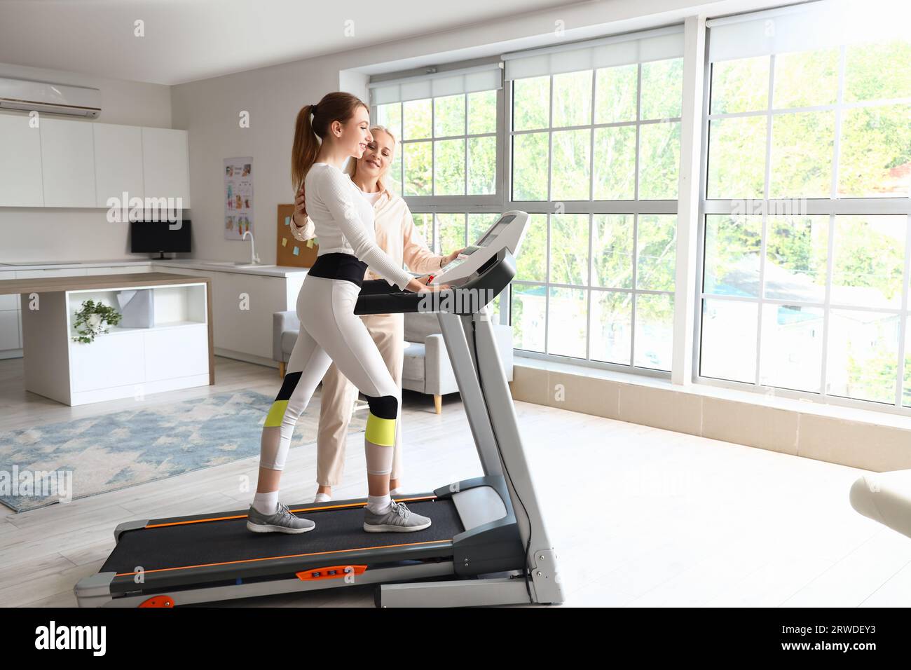Female physiotherapist working with young woman on treadmill in ...